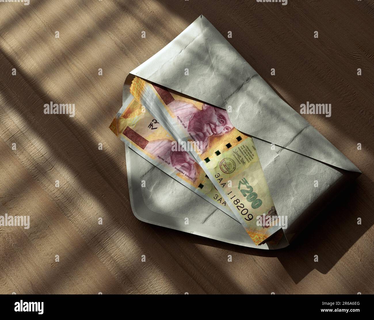 A spreading pile of rupee banknotes in an envelope on a wooden surface ...