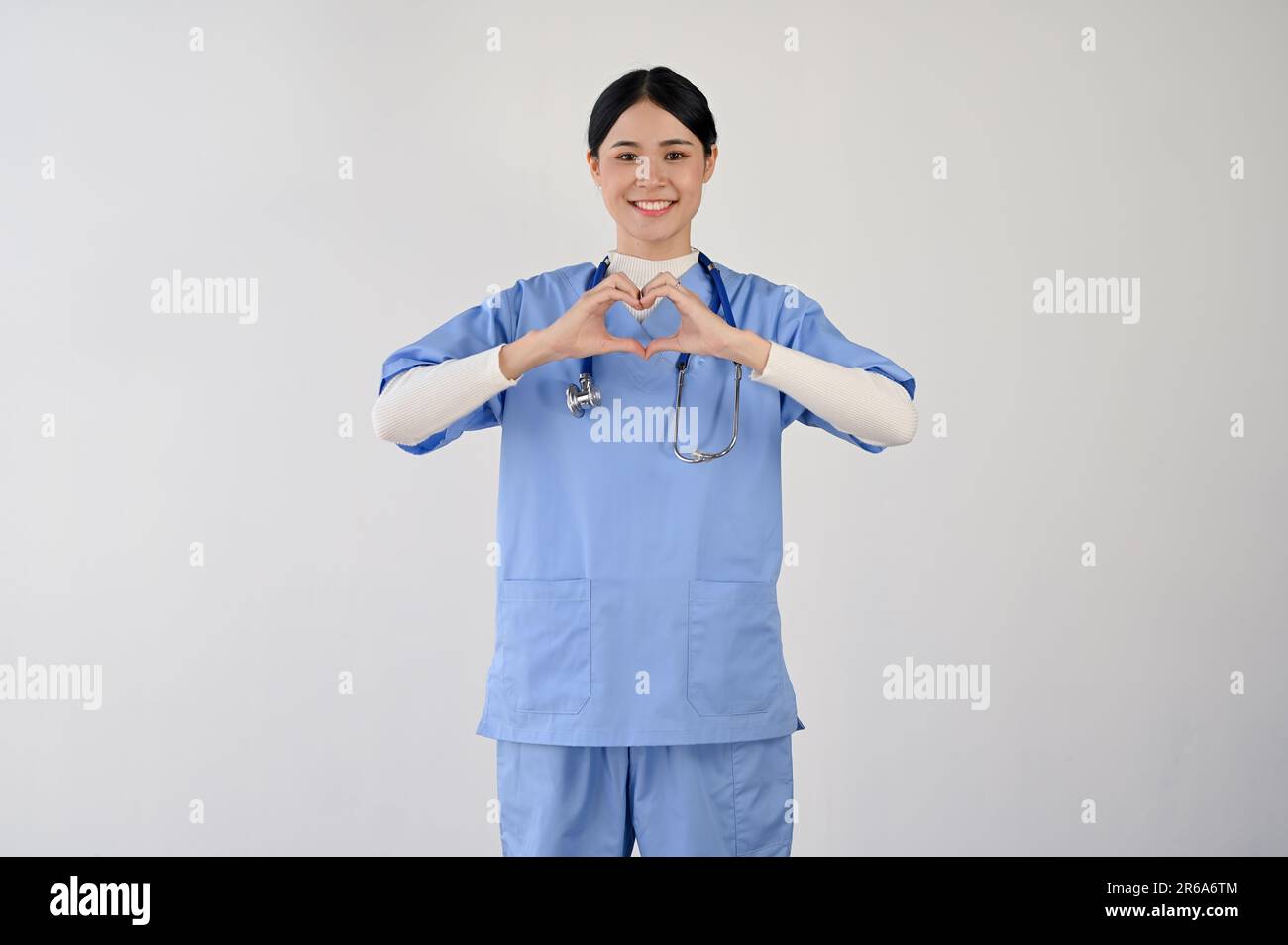 A positive and charming Asian female doctor in scrubs making a heart ...