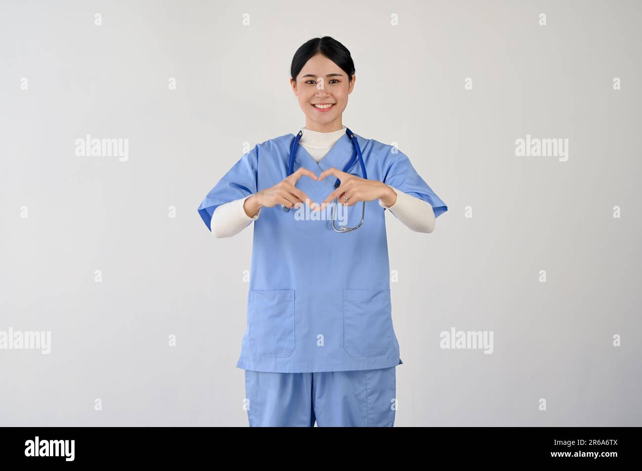 A positive and charming Asian female doctor in scrubs making a heart ...
