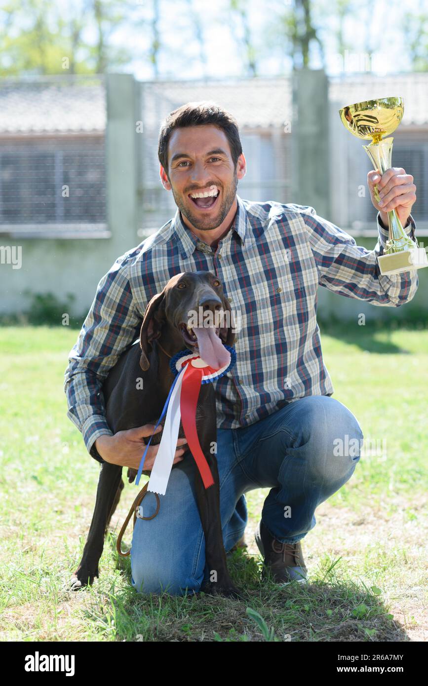 triumphant man holding trophy with dog wearing rosette Stock Photo - Alamy