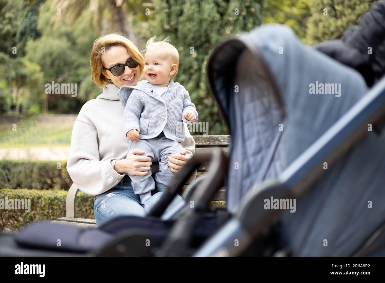 Mother sitting on bench in urban park, laughing cheerfully, holding her ...