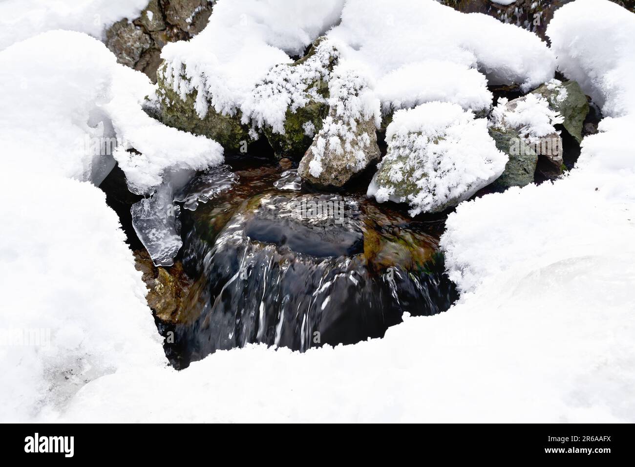 Spring water flowing from an iron pipe on a background of snow and ice ...