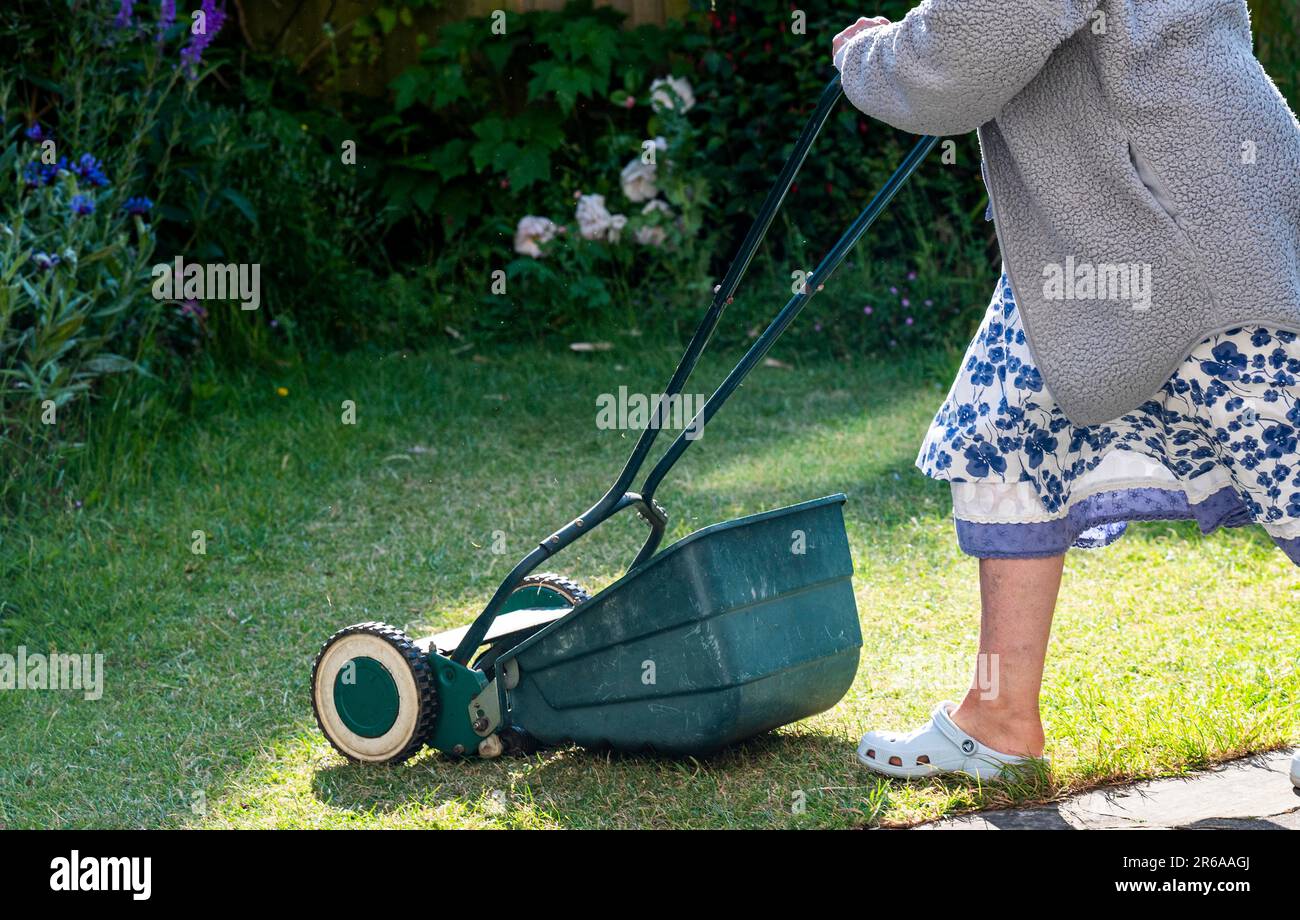 Woman using a hand mower cutting small city urban garden grass lawn ...