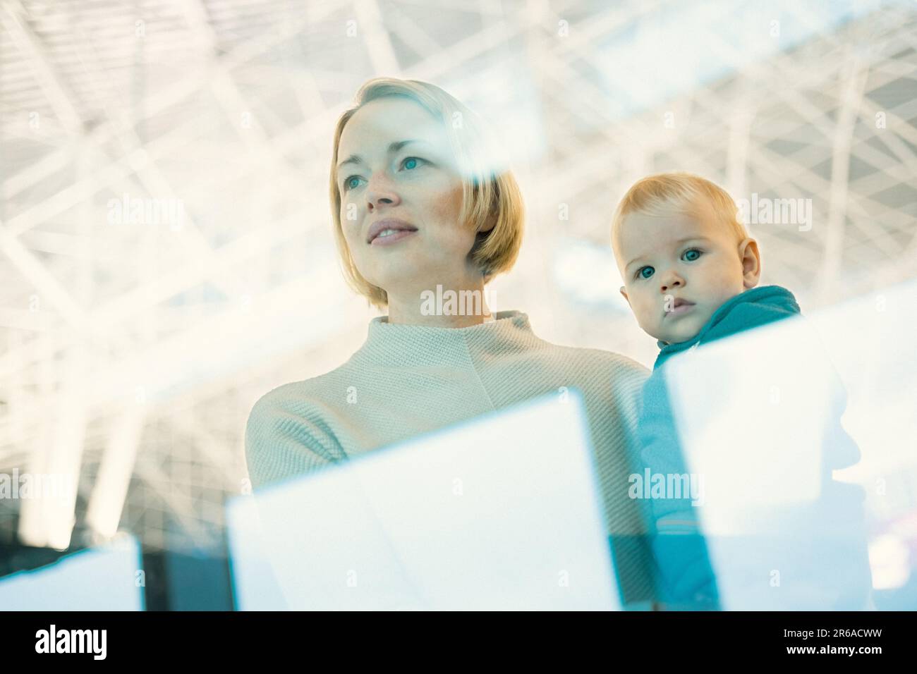 Thoughtful young mother looking trough window holding his infant baby ...