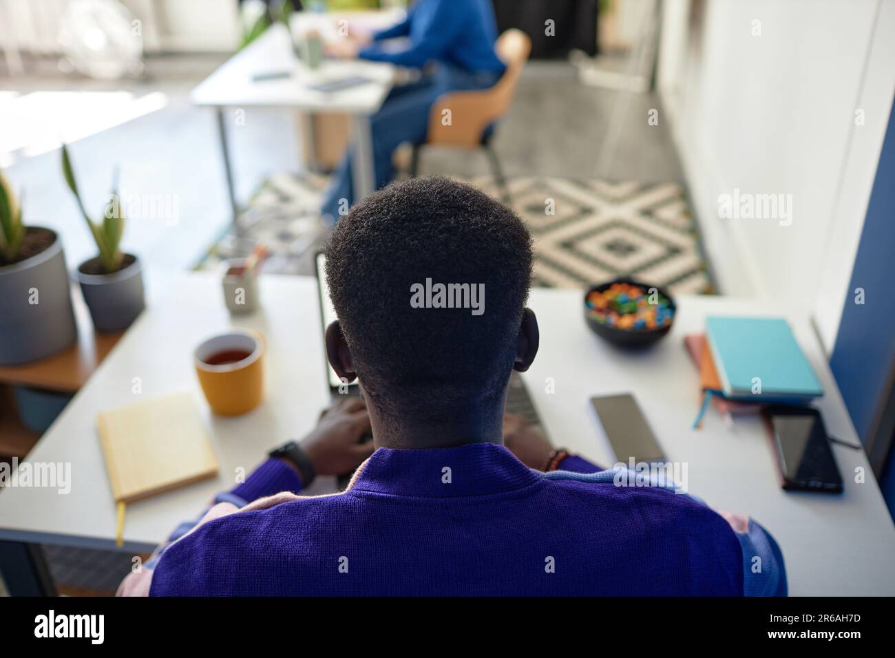 Back view at creative black man working at desk in fun non conventional ...