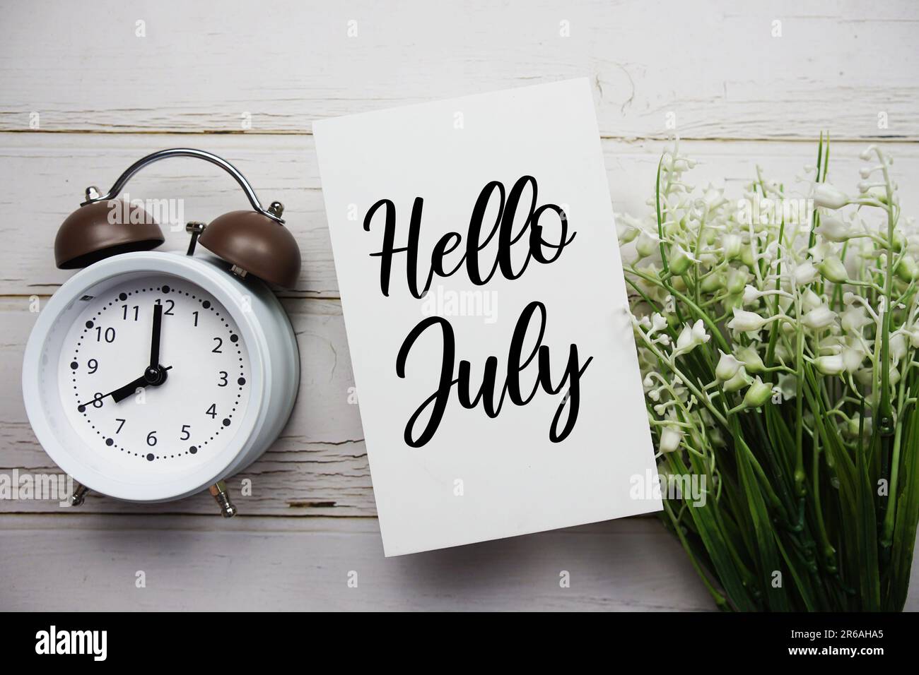 Hello July text message with flower and alarm clock on wooden ...