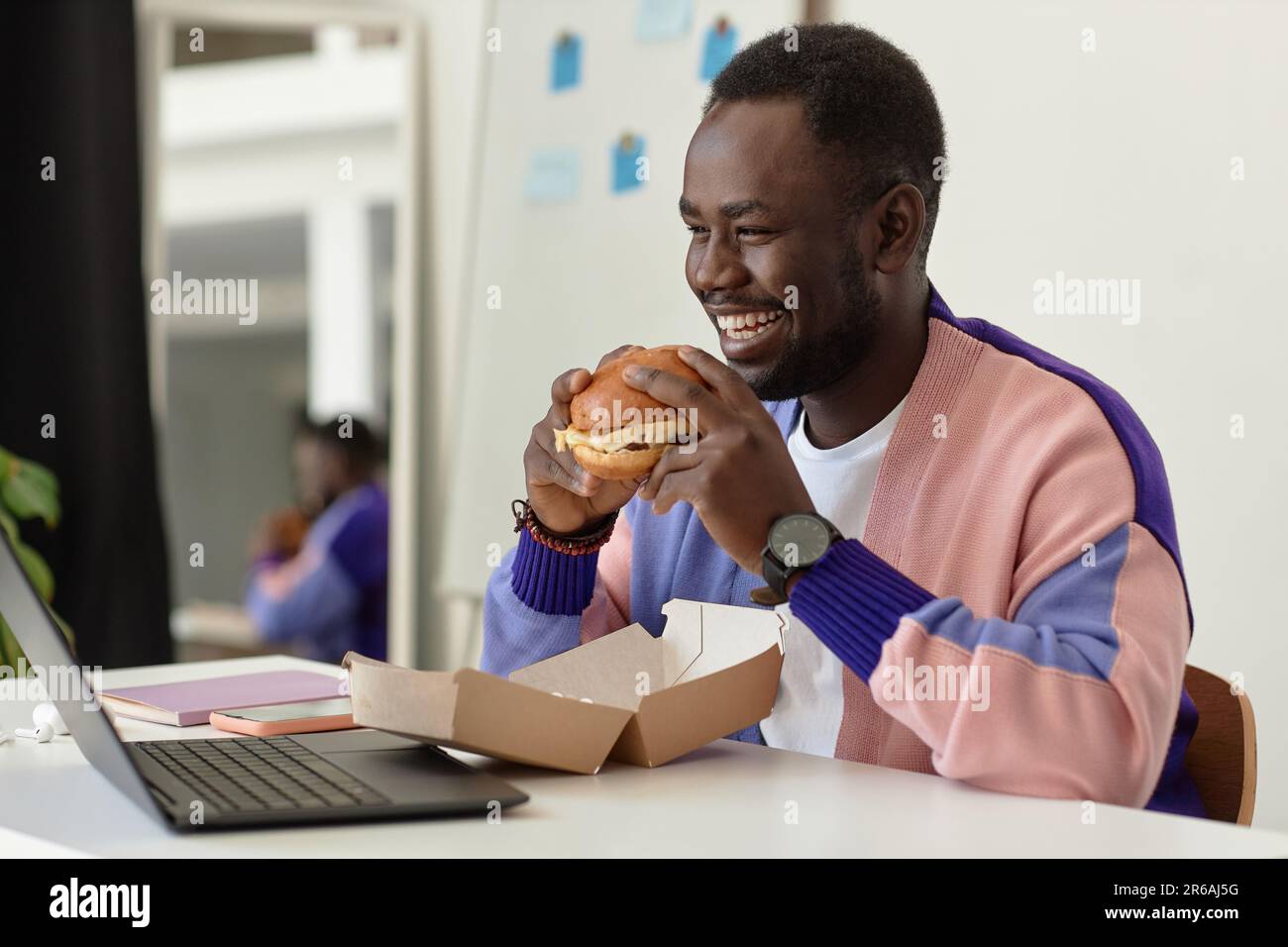 Side view portrait of smiling black man eating takeout burger at ...