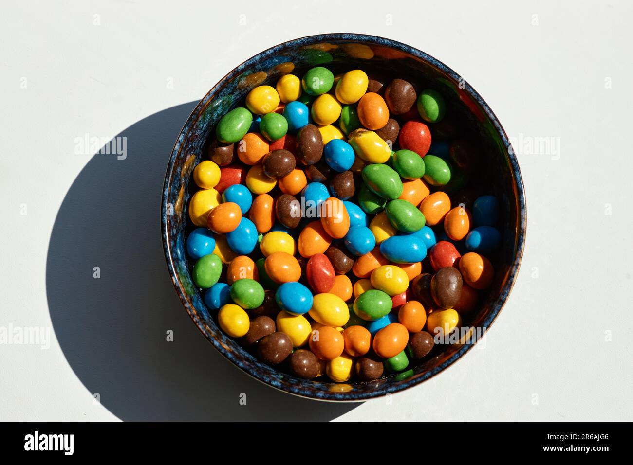 Minimal top view of colorful candy in bowl with harsh light and shadows ...