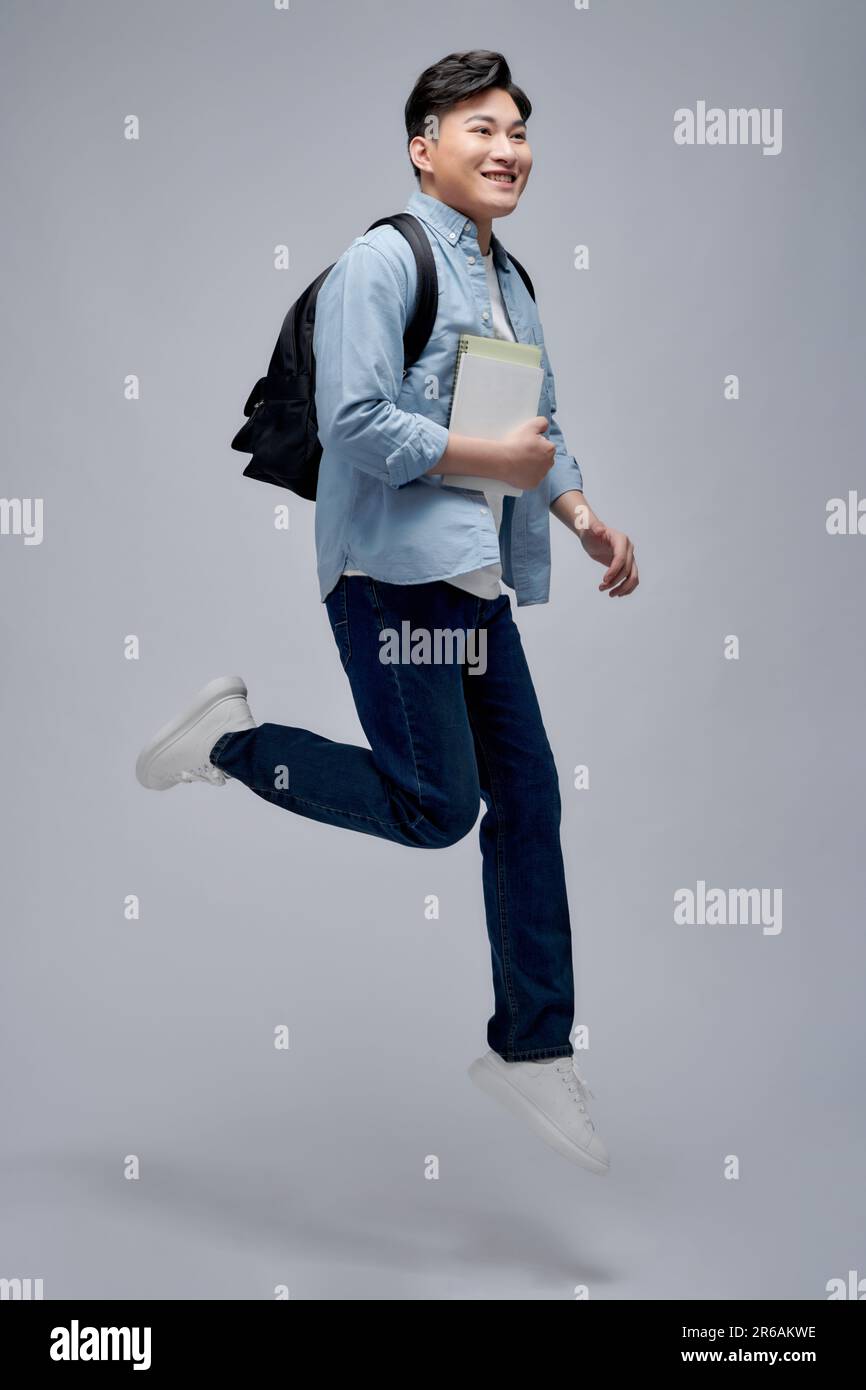 Full length of a smiling young asian man carrying backpack isolated ...