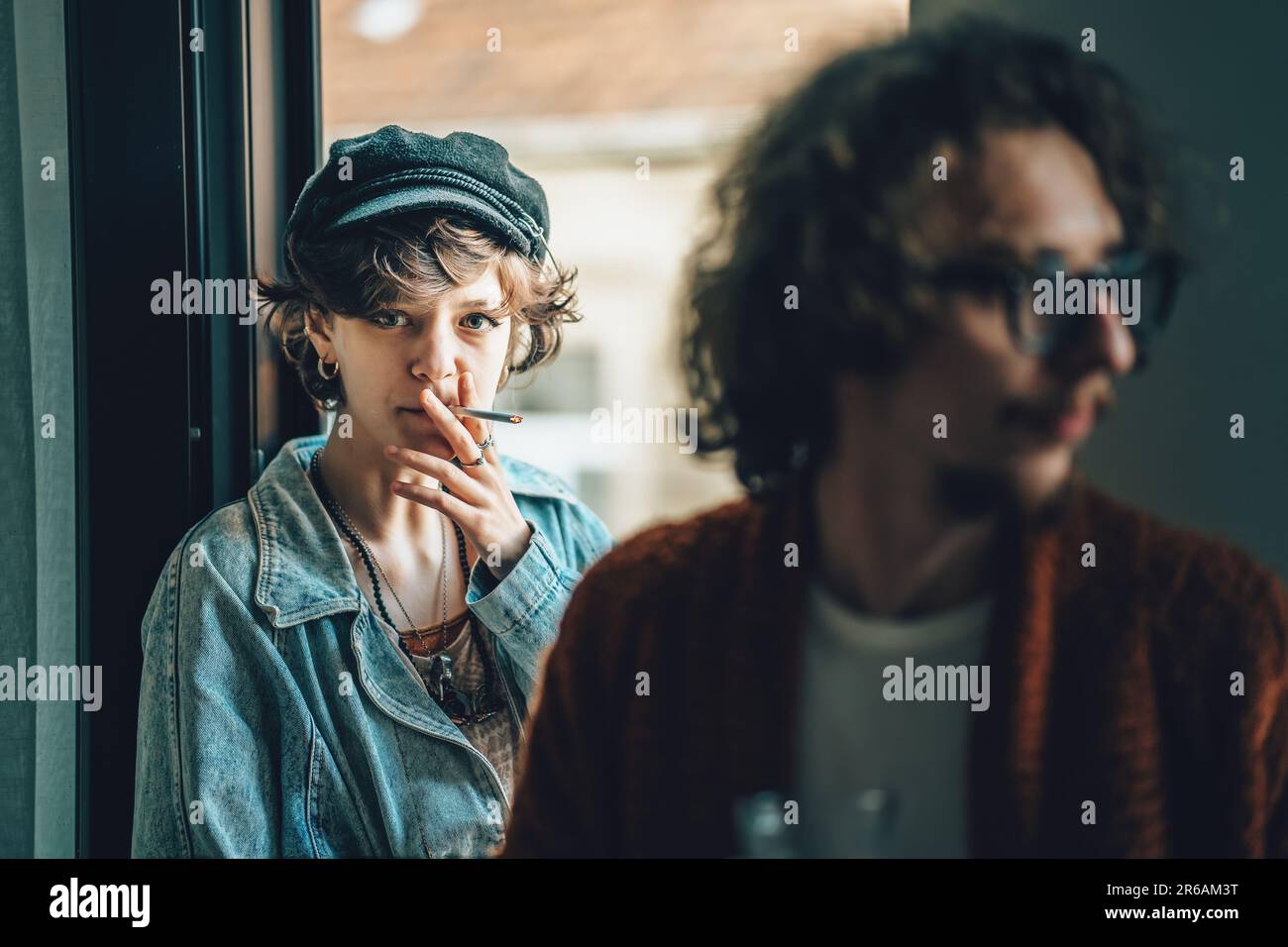 Smoking cigarette brunette woman in jeans jacket and defocused man ...