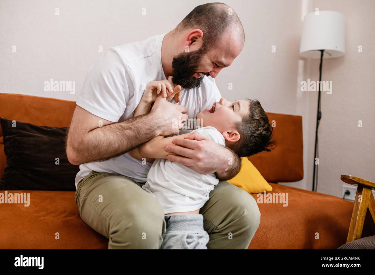 Father And Son Play Together Indoors Sit In Home Sofa Hug Cuddle And