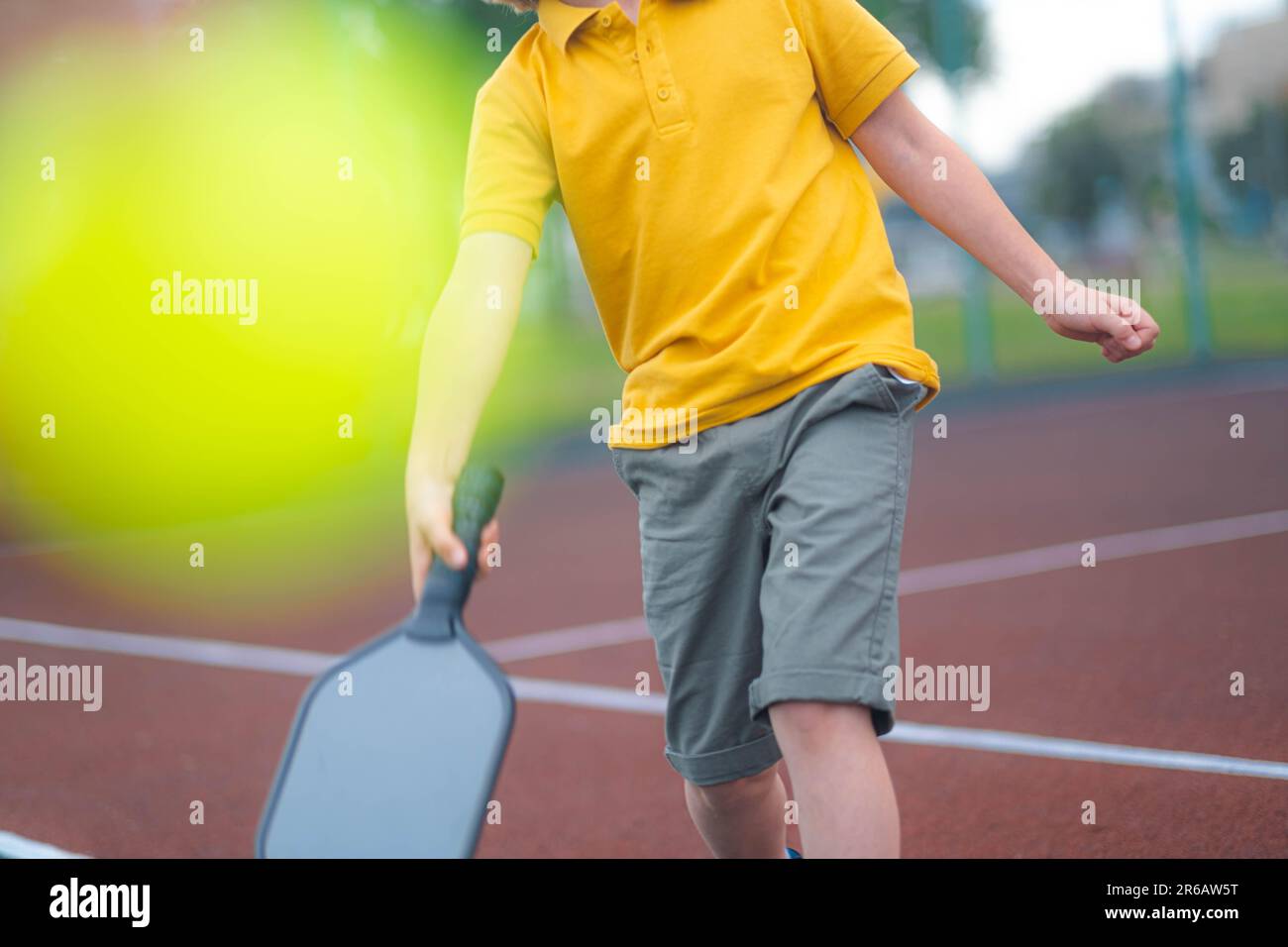 Happy blonde boy playing pickleball game, hitting pickleball yellow ...