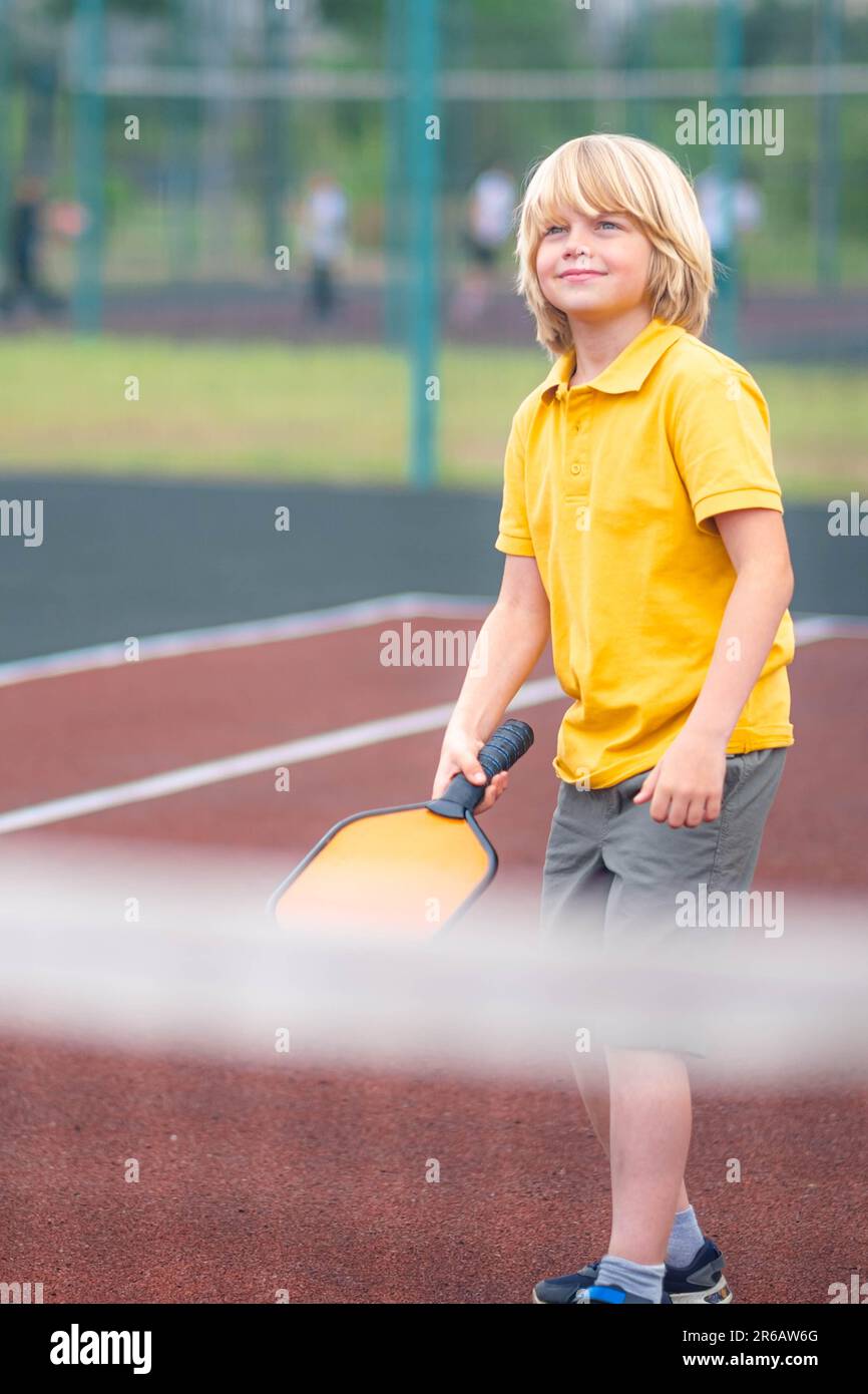 Happy blonde boy playing pickleball game, hitting pickleball yellow ...
