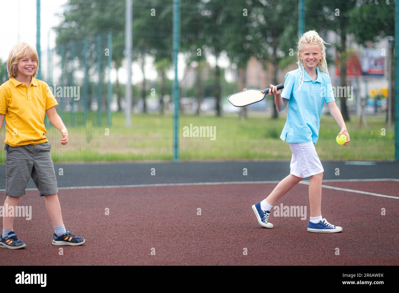 Laughing boy and girl playing pickleball game, hitting pickleball ...