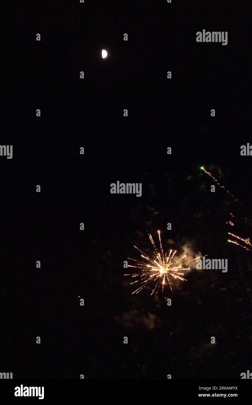 Small fireworks at night against black night sky with half moon, during ...