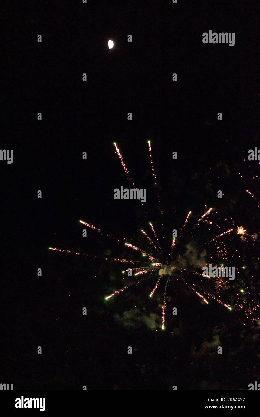 Small fireworks at night against black night sky with half moon, during ...