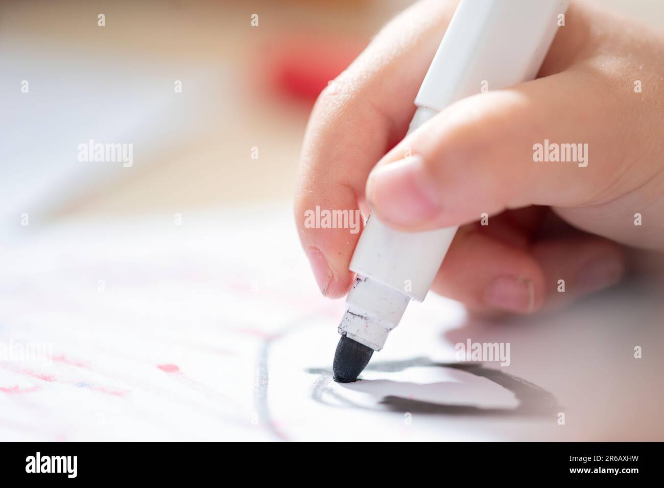 Hand of a small child drawing on a paper with a black felt-tip pen ...