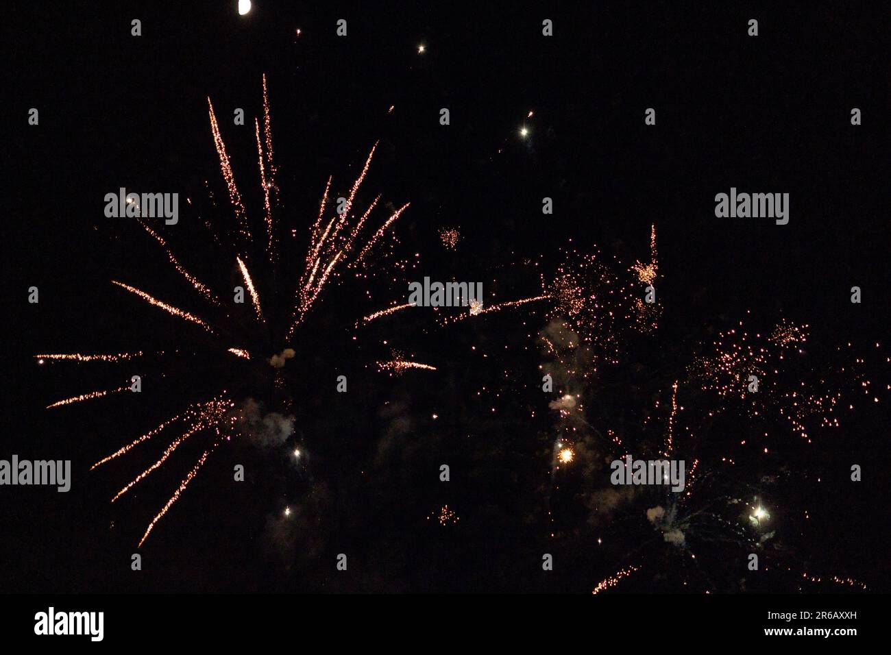 Small fireworks at night against black night sky with half moon, during ...