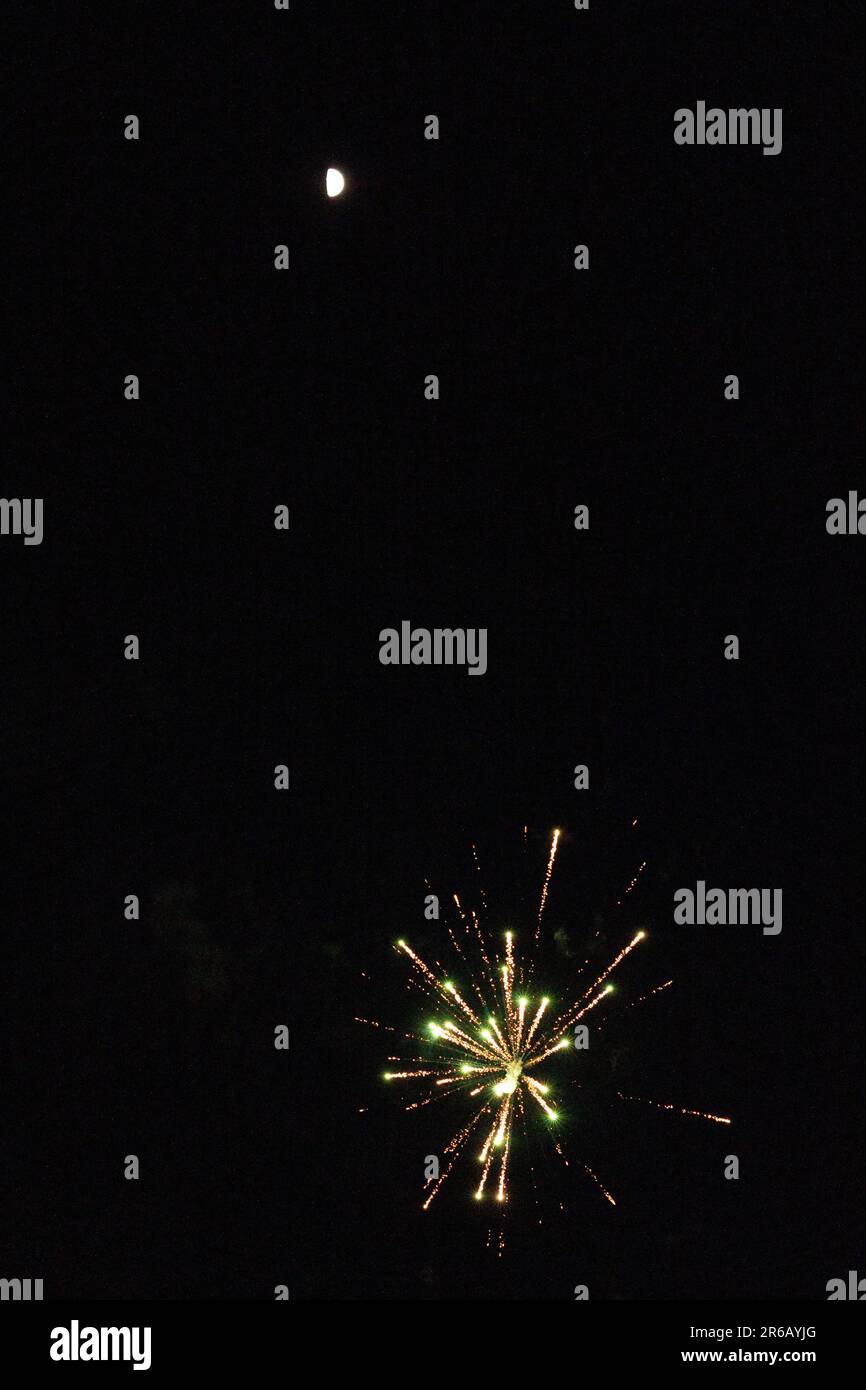 Small fireworks at night against black night sky with half moon, during ...