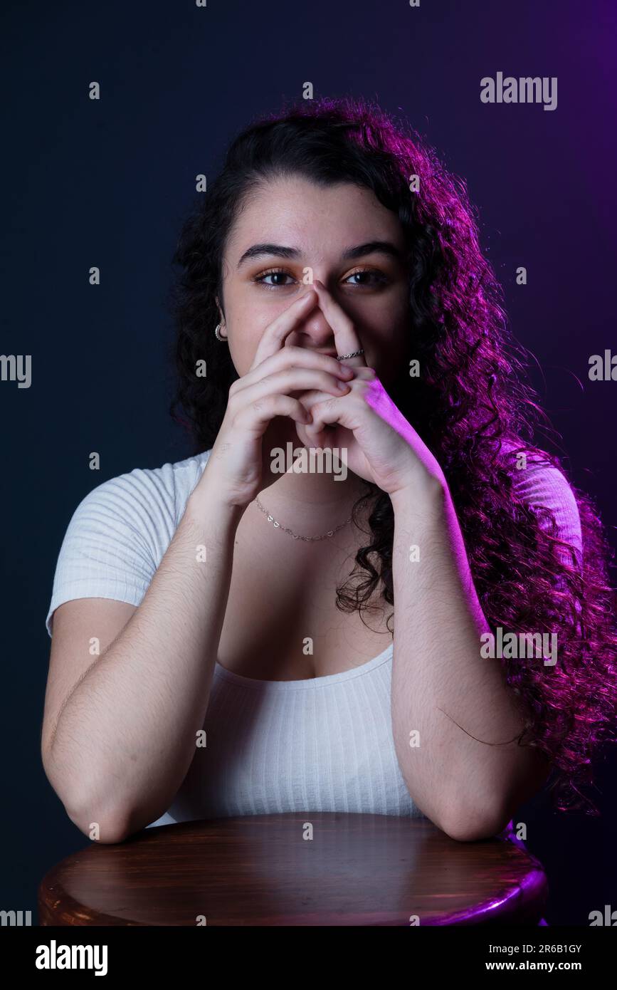 A young woman with curly hair and a, her hands resting on her face ...