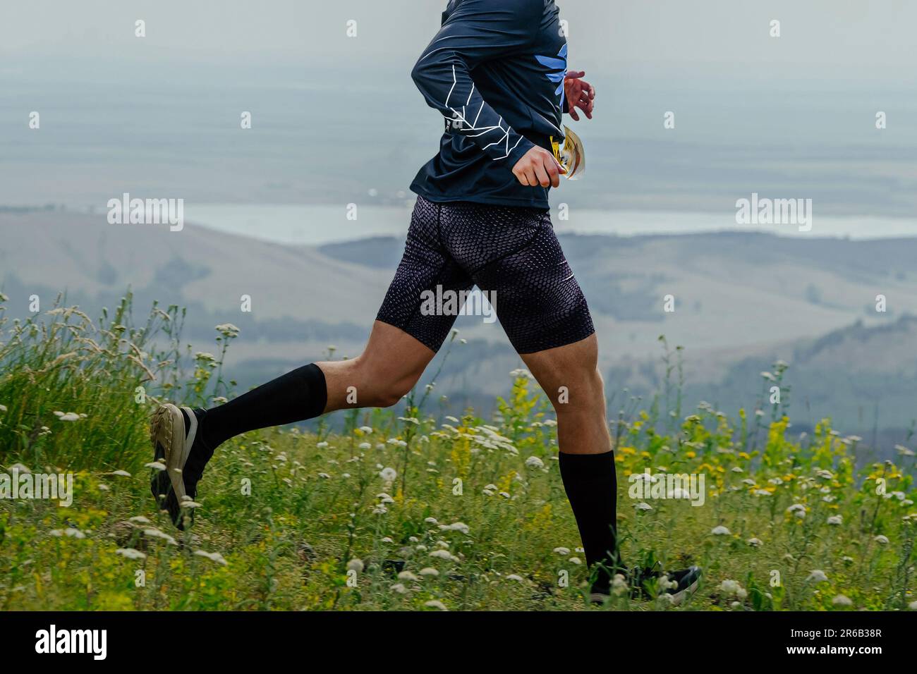 male runner running trail in green grass down mountain, summer marathon ...