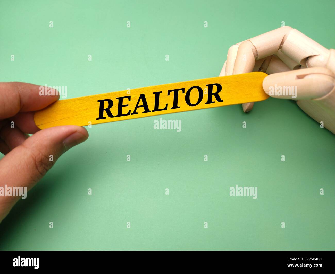 A close-up of two hands holding up a piece of wood with the word ...