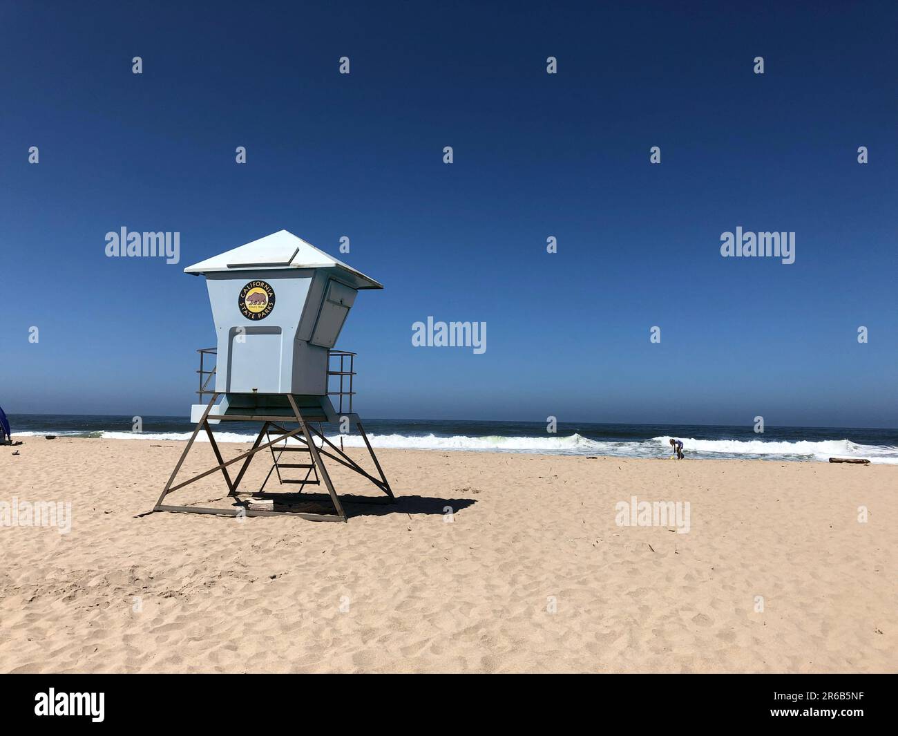A lifeguard tower stands in silhouette against a serene beach backdrop ...