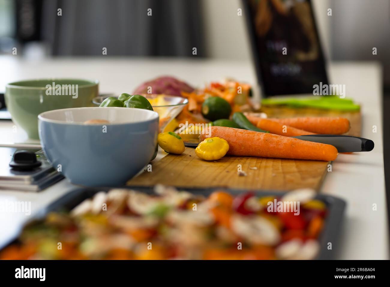 Ingredients, vegetables in baking tray and tablet on kitchen countertop ...