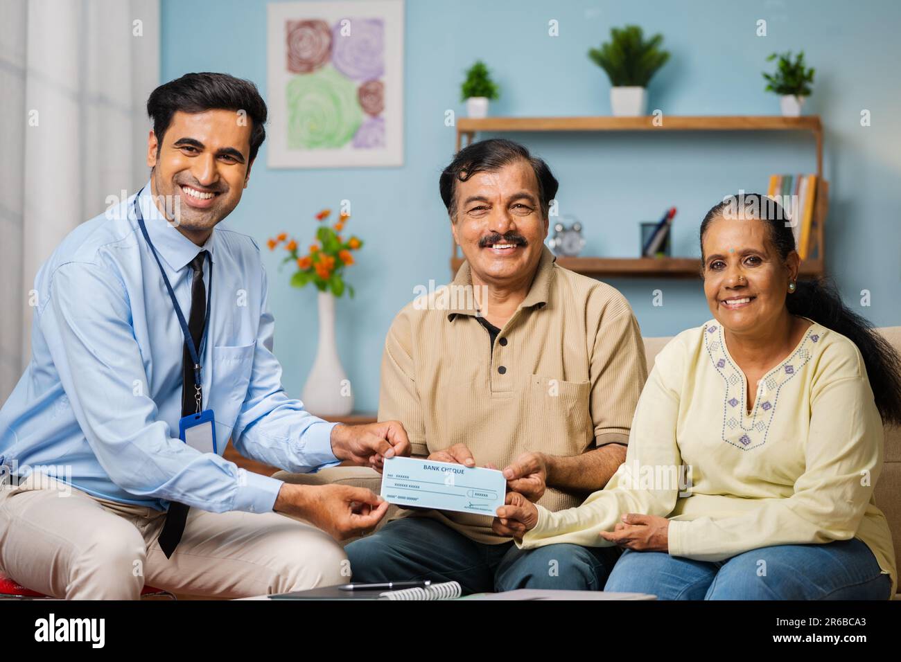 Happy smiling indian banker giving cheque to senior couple by looking ...