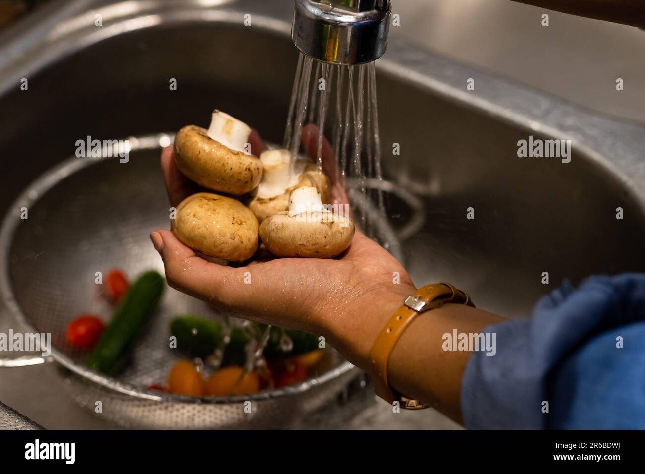Hand of biracial woman washing mushrooms and colander of vegetables in ...
