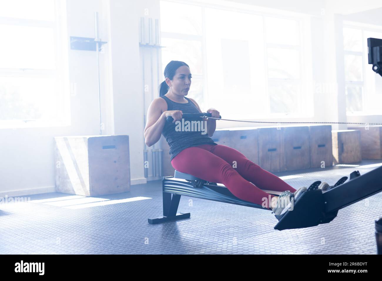 Dedicated caucasian young woman exercising on rowing machine against ...