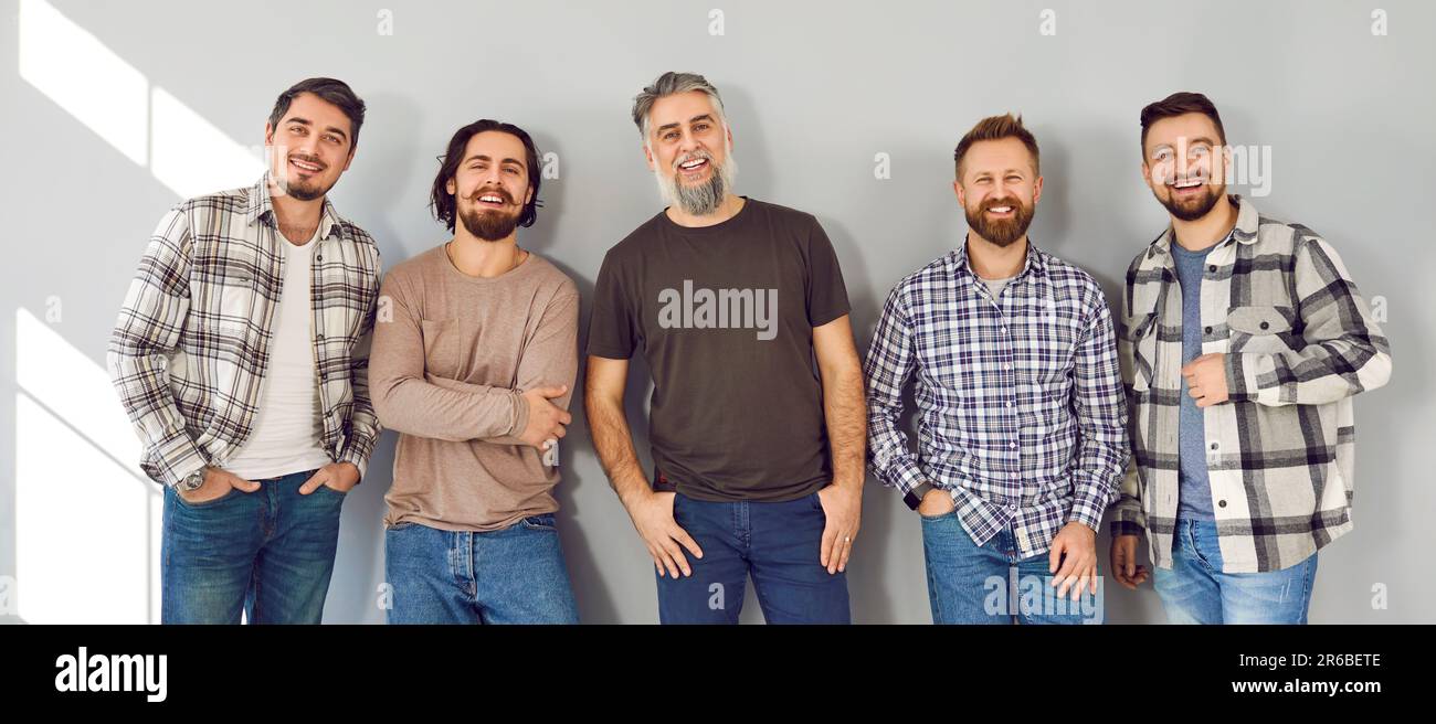 Group of happy men models wearing casual clothes standing by gray wall ...
