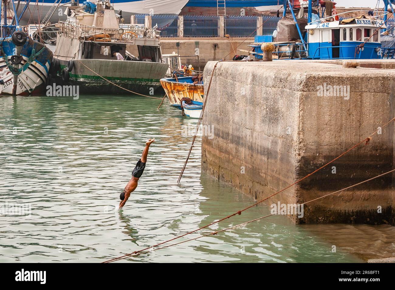 A man dives from the pier into the ocean waters. Essaouira, known as ...