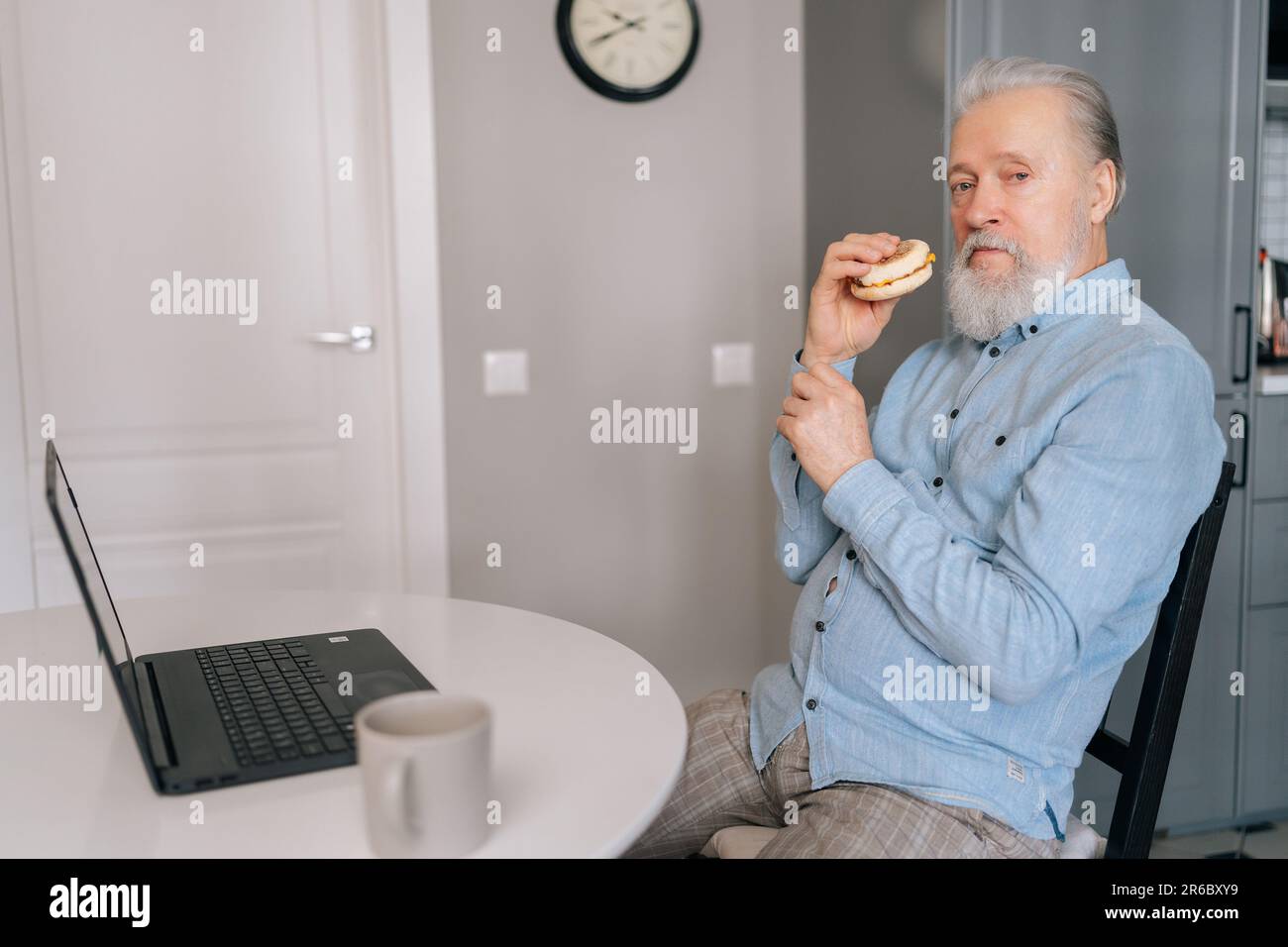 Hungry bearded senior older businessman eating hamburger with beef from ...