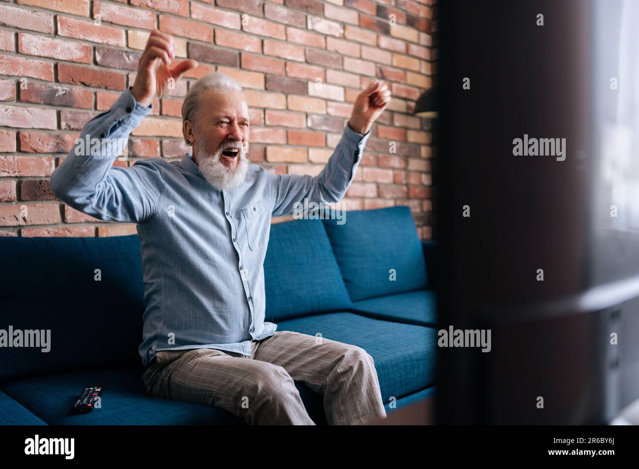 Overjoyed happy grey-haired mature football fan raising arms ...