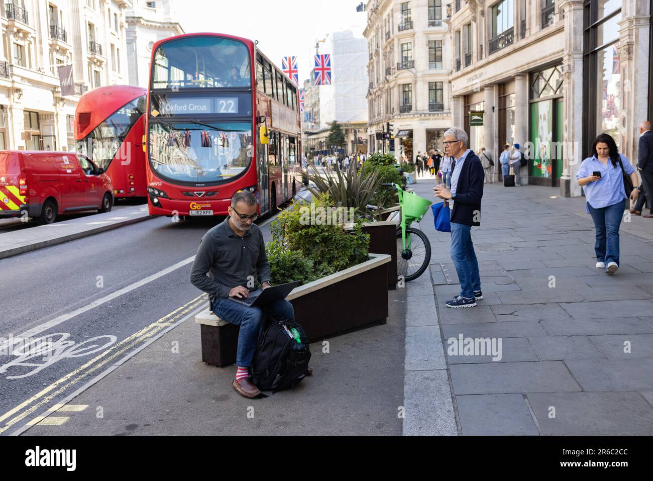 A man works on his laptop computer whilst sitting on a raised flower ...