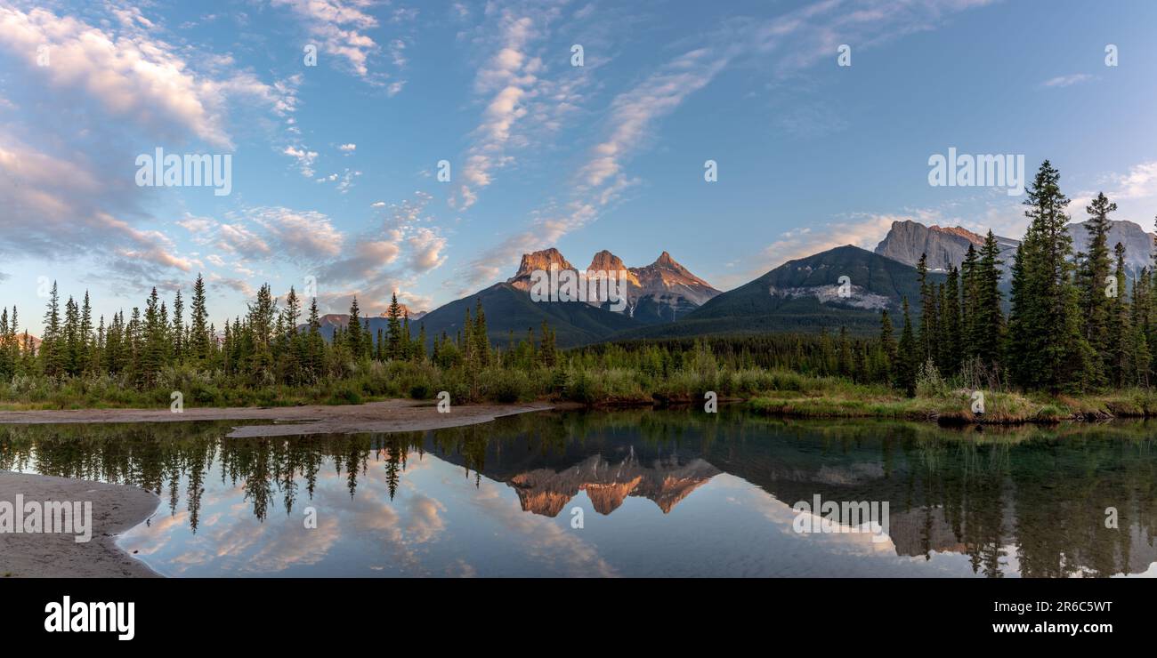 Mountain peaks reflecting in the calm water below at Three Sisters in Canmore, near Banff ...