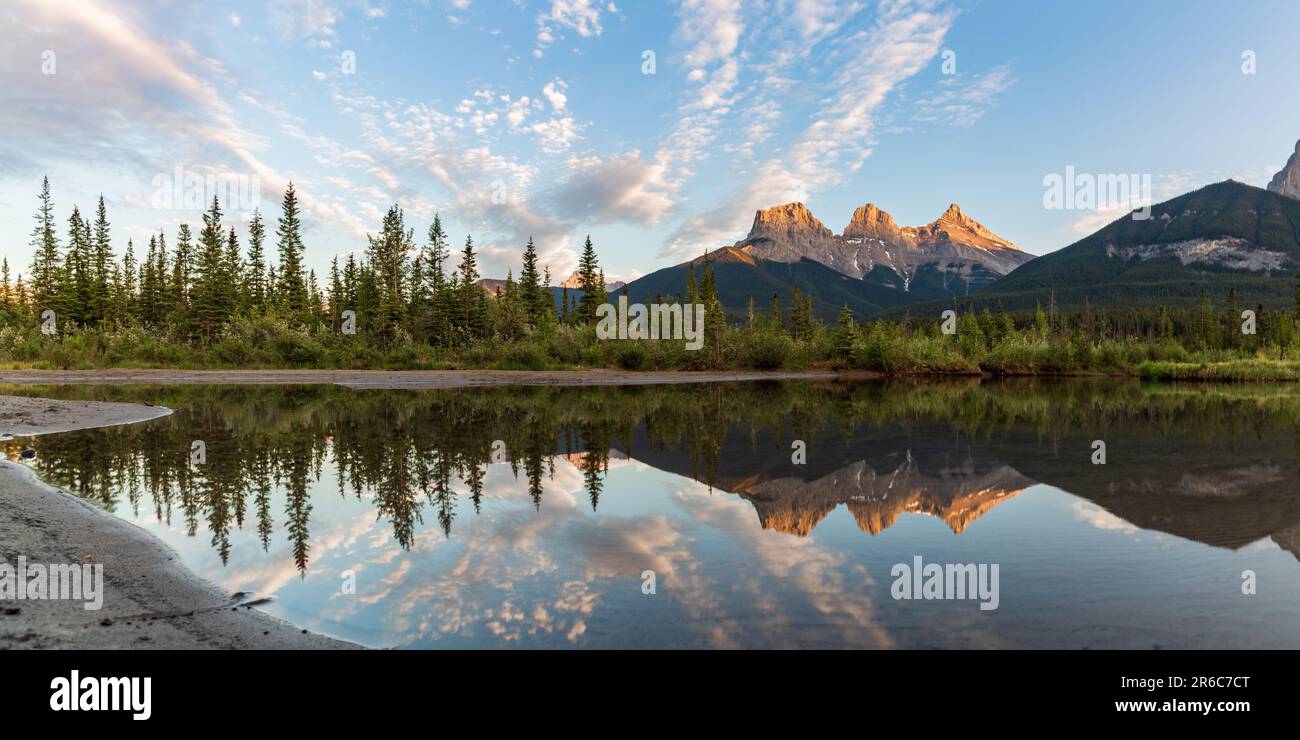 Mountain peaks reflecting in the calm water below at Three Sisters in Canmore, near Banff ...