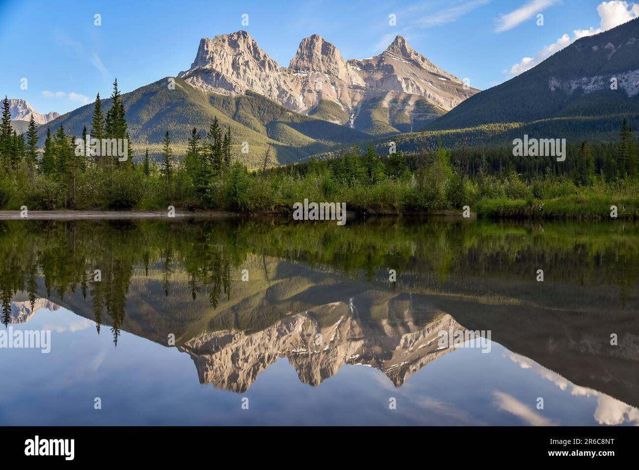 Mountain peaks reflecting in the calm water below at Three Sisters in Canmore, near Banff ...