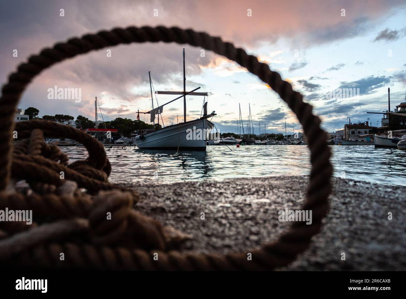 A small boat is moored in a calm body of water, with a rope tied to a ...