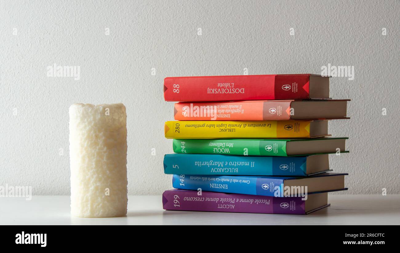 A still life setting featuring a collection of books, a lit candle, and ...