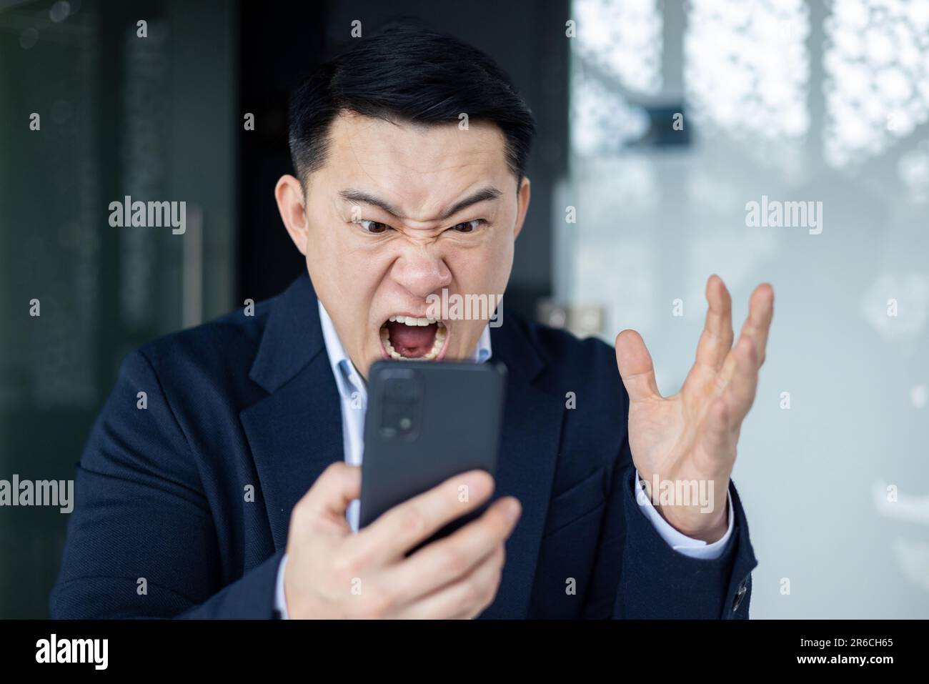 Close-up of angry asian man yelling at phone screen, boss at workplace ...