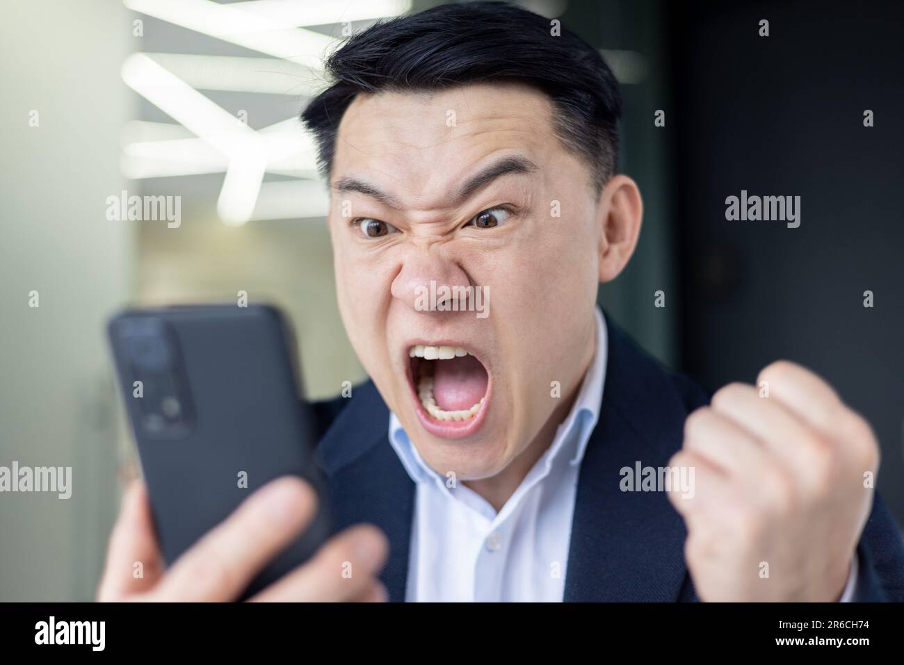 Close-up of angry asian man yelling at phone screen, boss at workplace ...