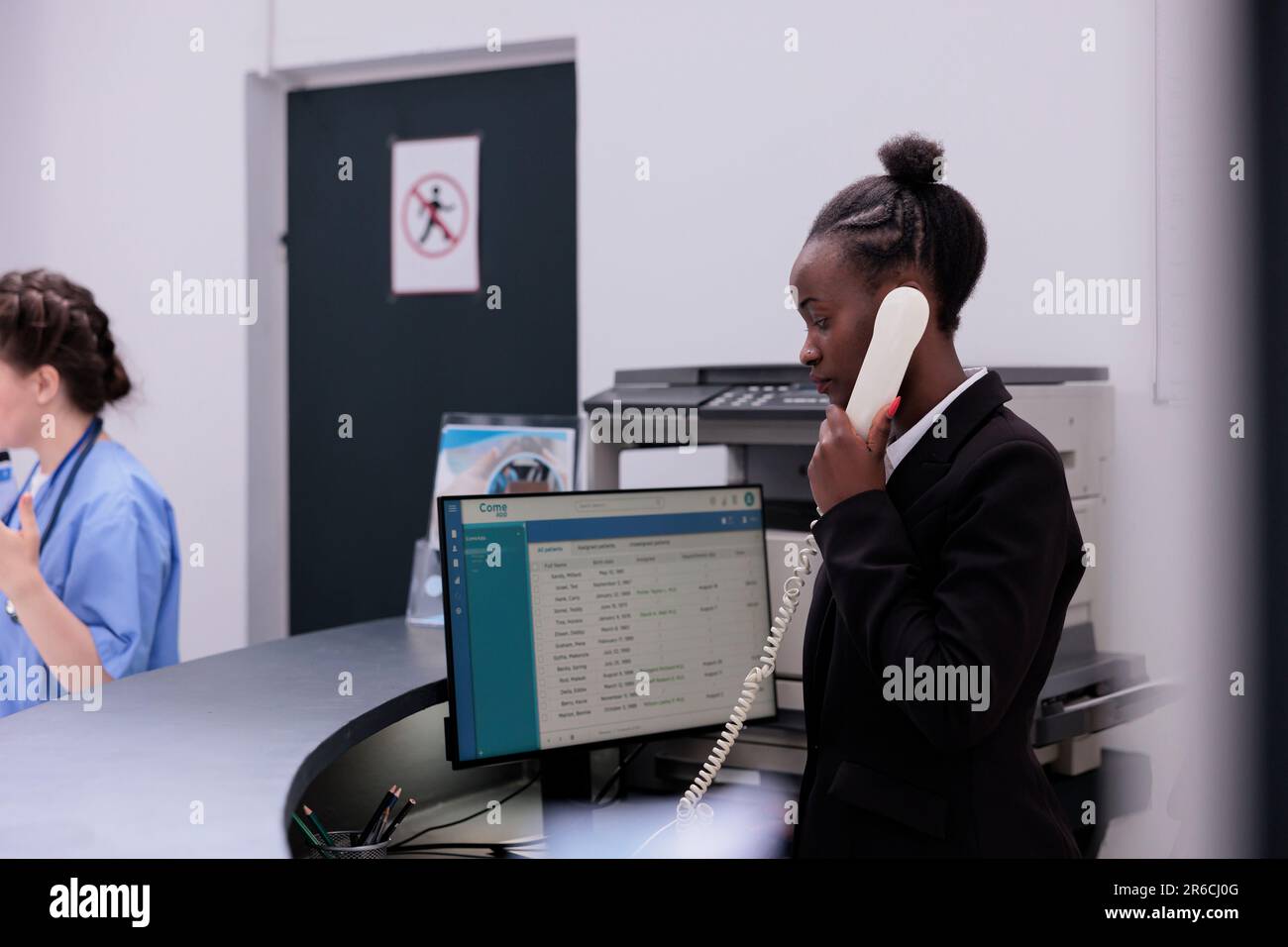 Receptionist talking at landline phone with remote patient discussing ...