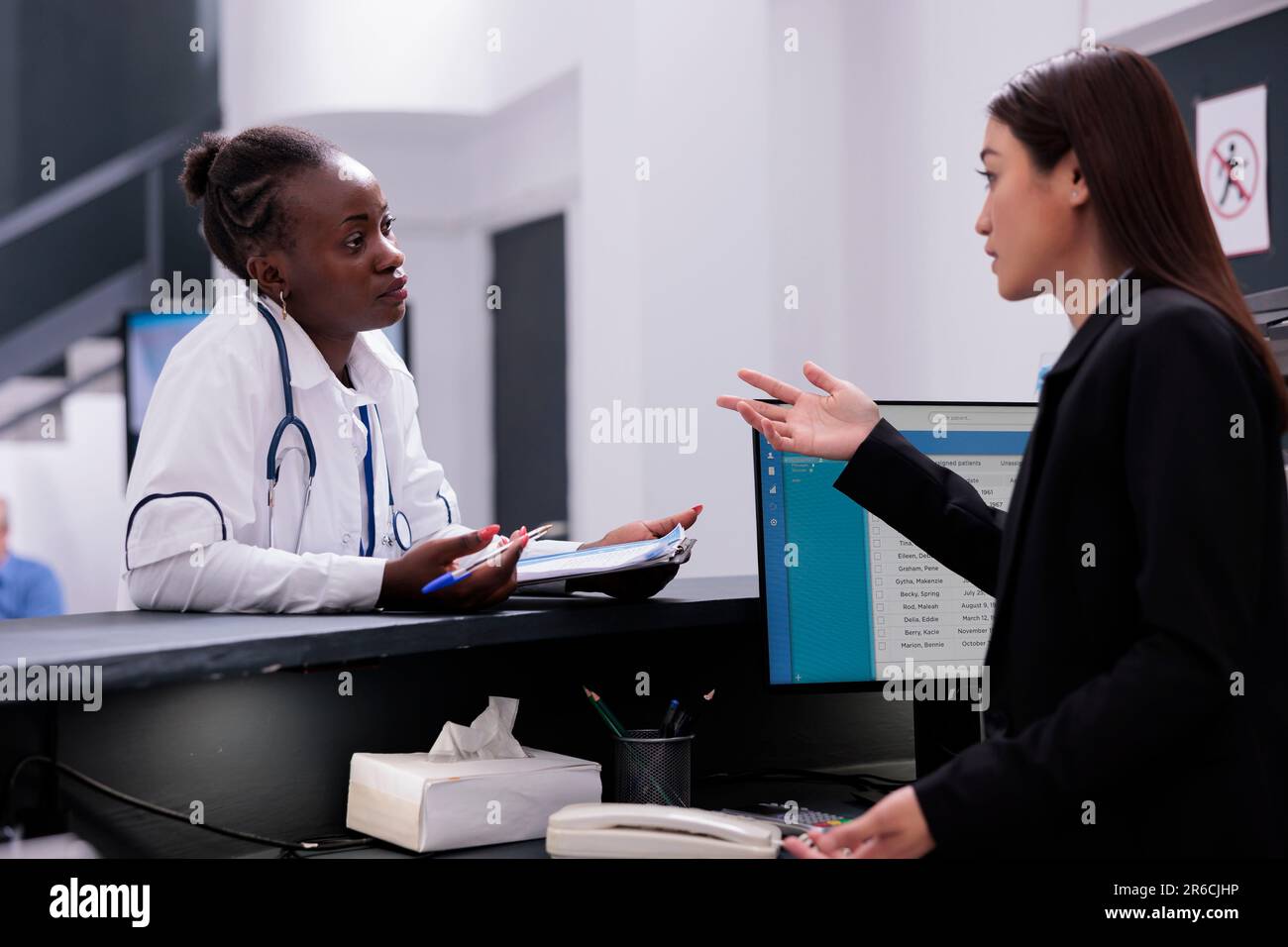 Asian receptionist talking with specialist doctor at hospital reception ...