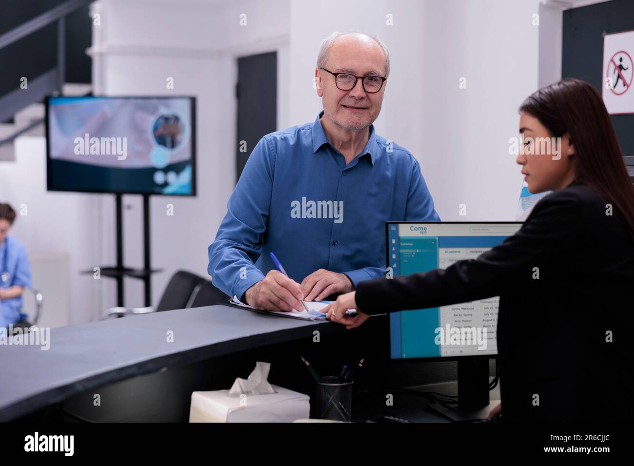 Receptionist showing medical report to old patient putting him to sign ...