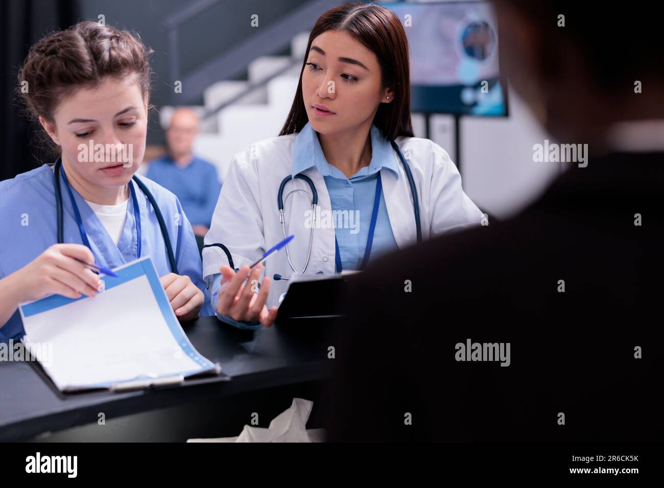 Diverse medical staff standing at reception desk discussing patient ...
