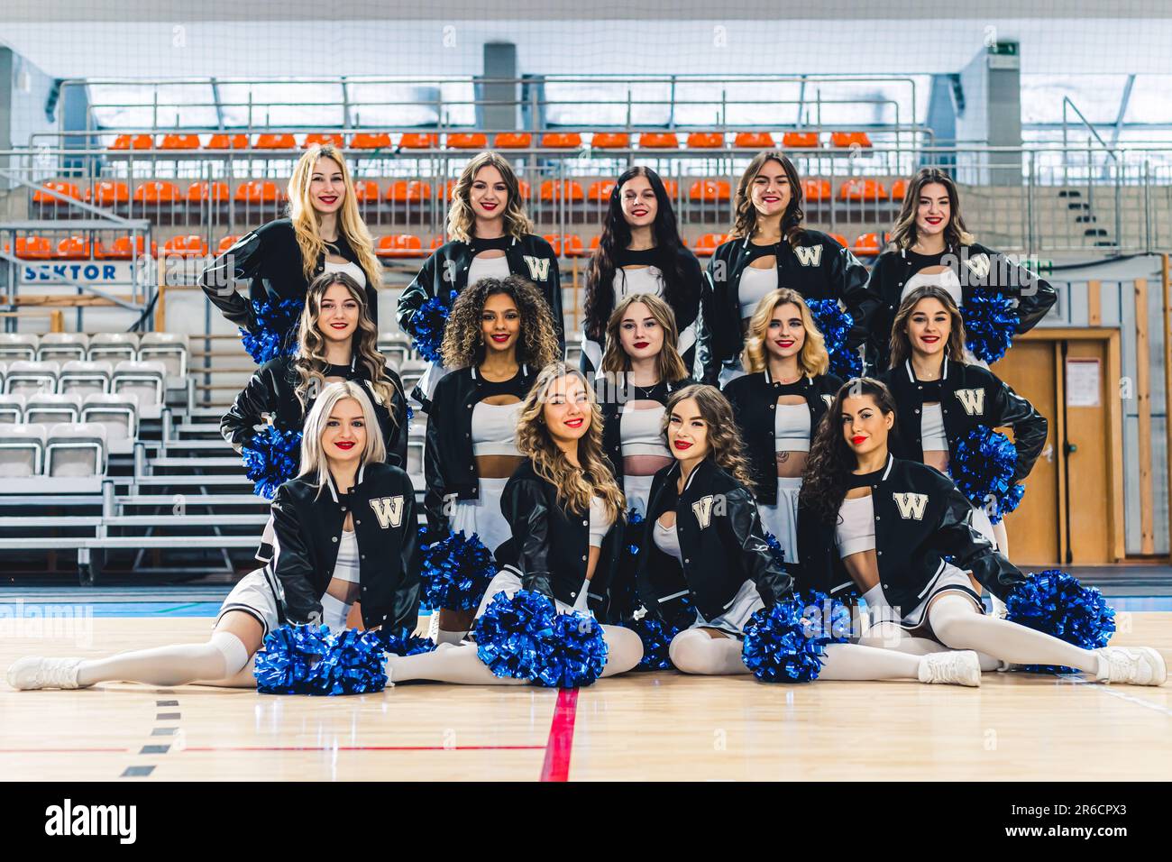 Smiling cheerleaders team posing for a picture with blue pompons on a court. High quality photo ...