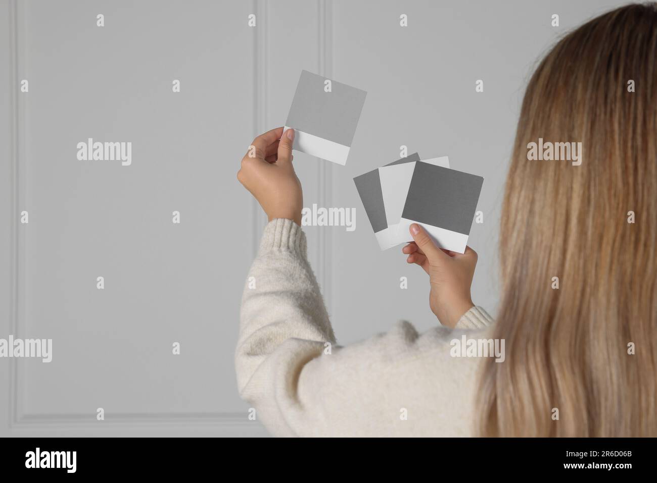 Woman choosing paint shade for wall indoors, focus on hands with color ...