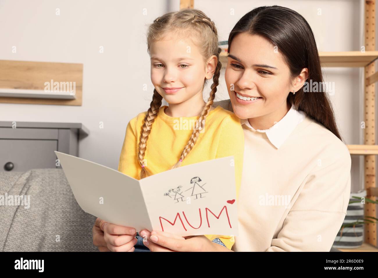 Happy woman receiving greeting card from her little daughter at home ...